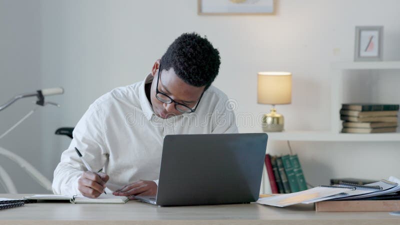 Black Business Man Writing Notes while Working Remotely on Laptop ...