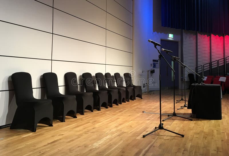 Black Chairs Against a White Wall and Microphones on a Stage Set Up ...