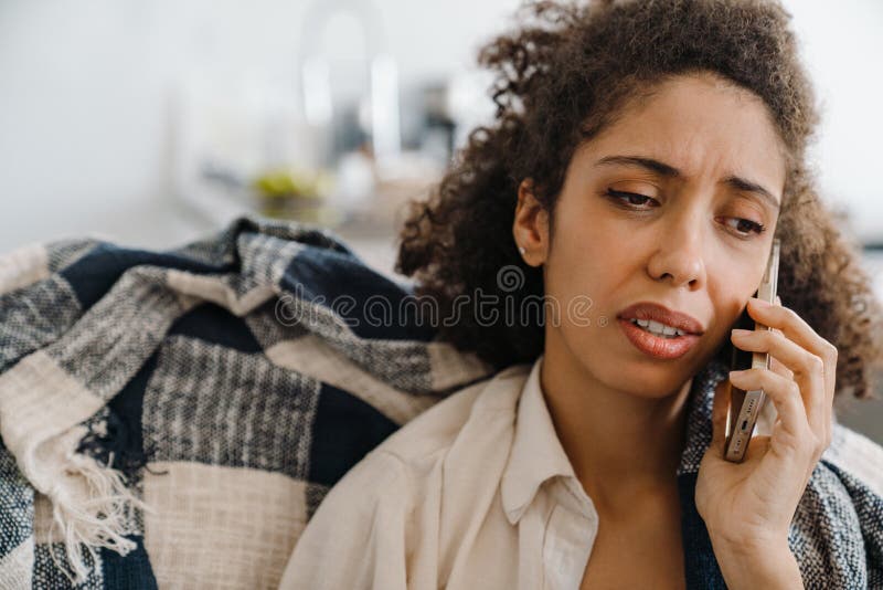Black Displeased Woman Talking On Mobile Phone While Sitting On Sofa