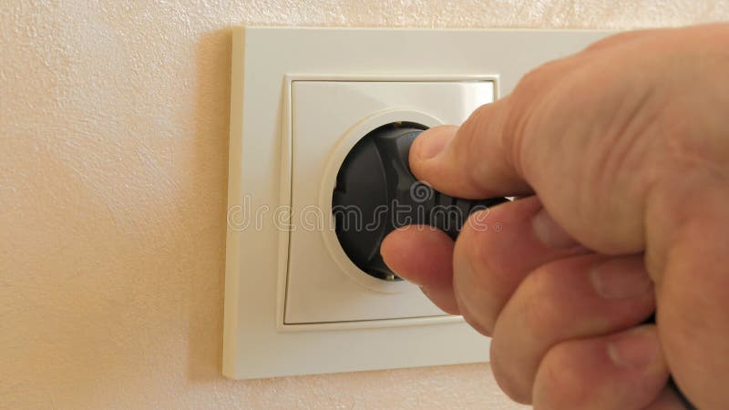 A Black Electric Plug with a Wire is Pulled Out from a White Socket by ...