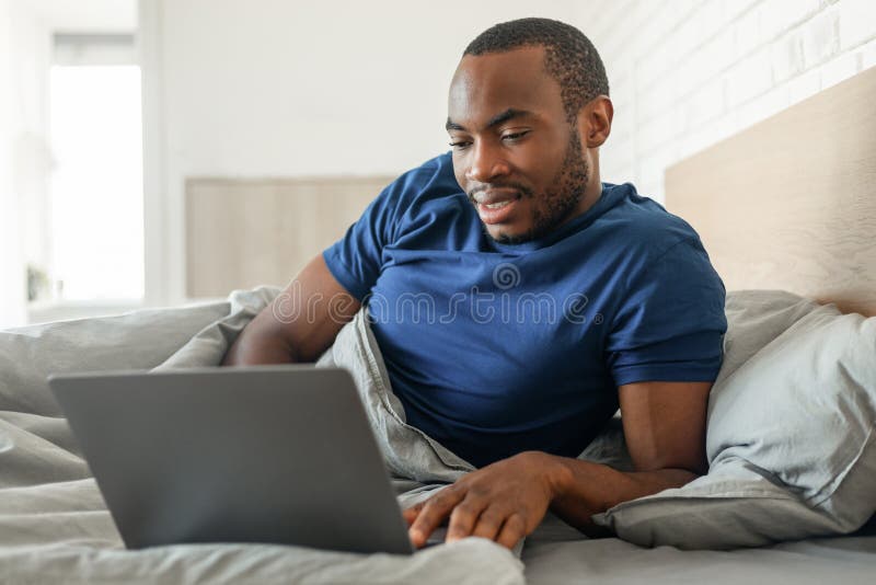 Black Freelancer Guy Using Laptop Working Online Lying in Bedroom Stock ...