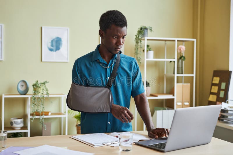 Black Man with Arm Sling Working at Standing Desk Using Laptop in ...