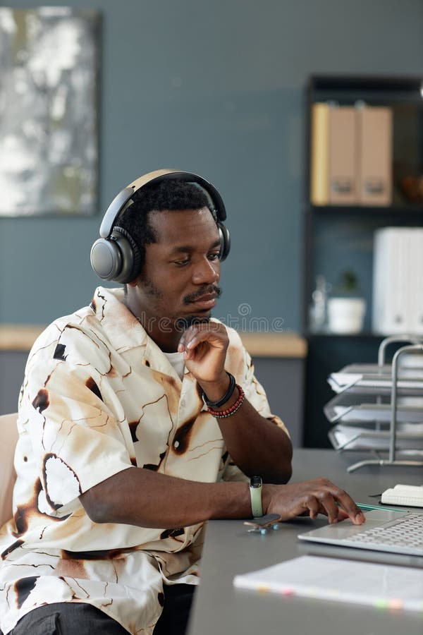 Black Man Using Computer in Headphones Looking at Screen with Bored ...
