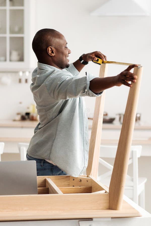 Black Millennial Handyman Assembling Wooden Table and Measuring the ...