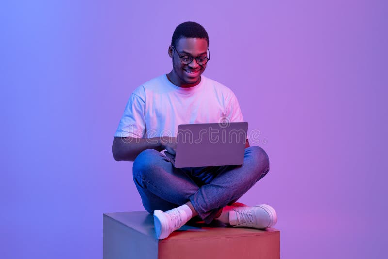 Black Programmer Guy Using Laptop Computer, Sitting on Cube in Neon ...
