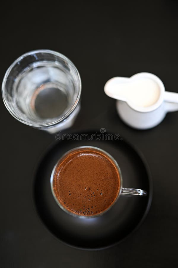 Black Table with a Cup of Coffee, a Portion of Milk and a Cup of Water ...