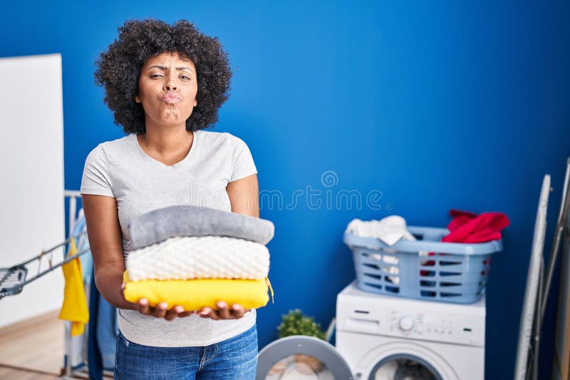 Black Woman With Curly Hair Holding Clean Laundry Looking At The Camera