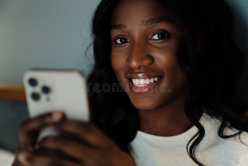 Black Woman Smiling and Using Mobile Phone while Lying in Bed at Home ...