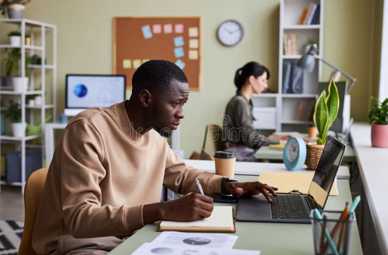 Black Young Man Working at Desk in Office and Taking Notes Writing in ...