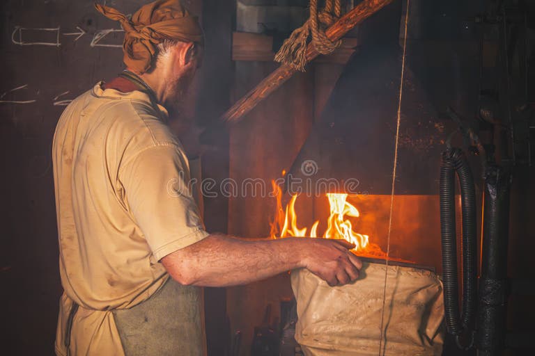 Blacksmith in an Authentic Forge Fans the Fire with Hand-held Bellows ...