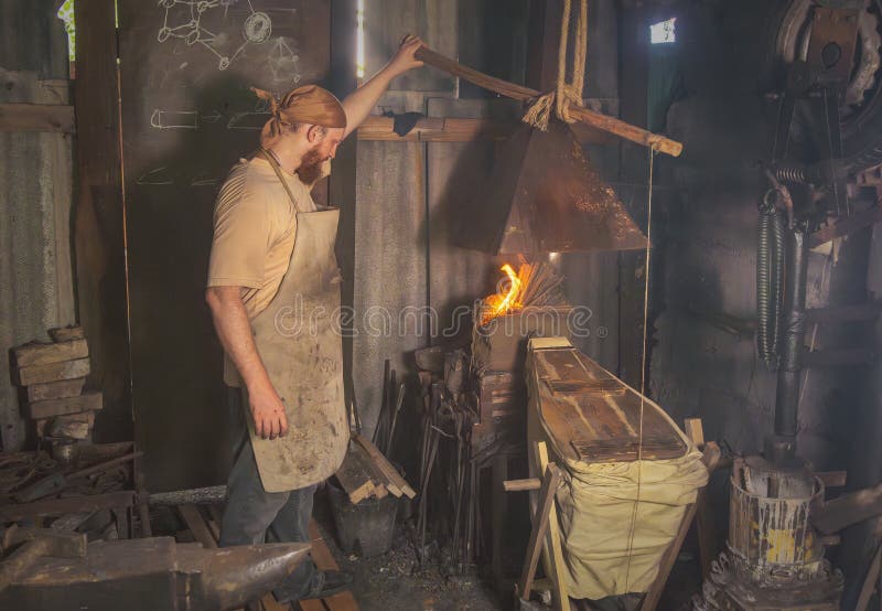 Blacksmith in an Authentic Forge Fans the Fire with Hand-held Bellows ...