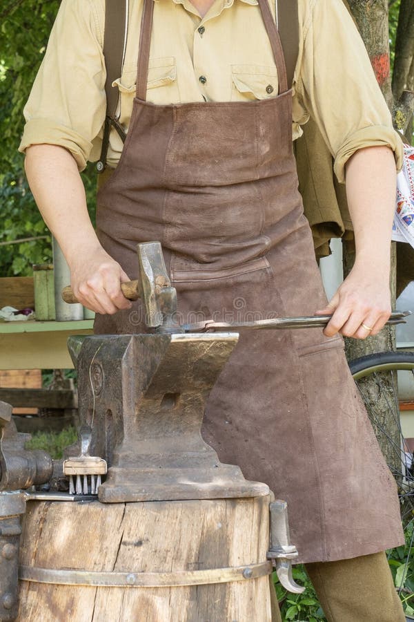 A Blacksmith in a Brown Leather Apron is Forging a Piece of Iron on an ...