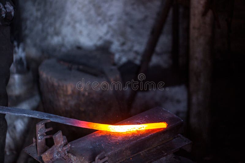 In a Blacksmith`s Workshop. Blacksmith in One Hand Hold a Workpiece of ...
