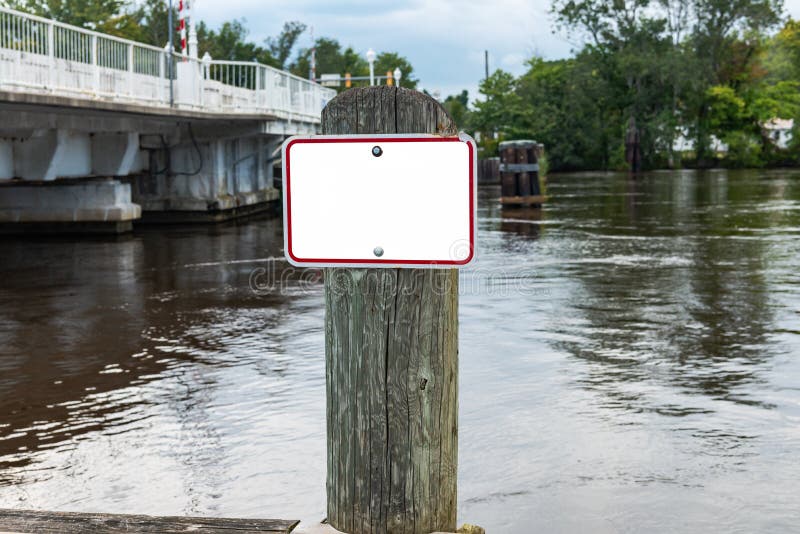 Blank White Sign Attached To a Wooden Post with a River and a Bridge ...