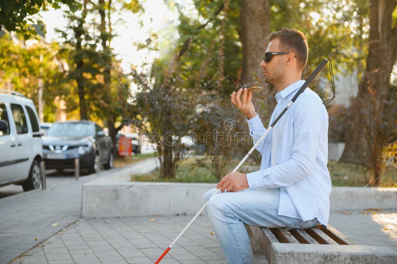 Blind Man with a Walking Stick Sits on a Bench Uses a Smartphone on the ...