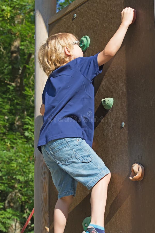 A Boy Climbs the Top of a Climbing Wall in a Sports Park Climbing Wall ...