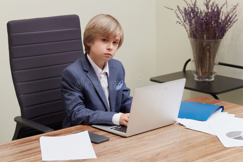 The Blond Boy Works in the Office for a Laptop and Looks at the Camera ...