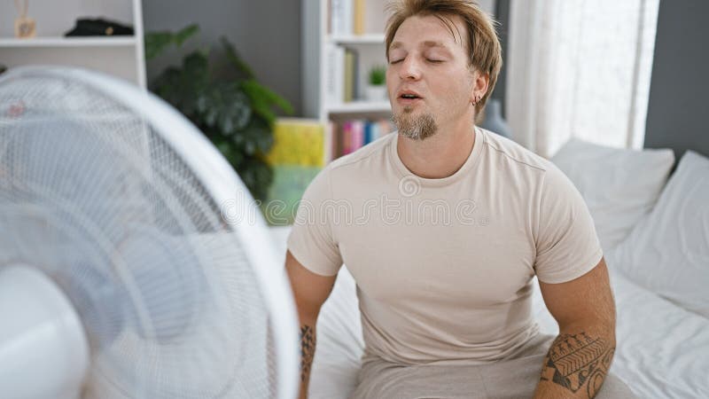 Blond Man with Beard Enjoys Cooling Breeze from Fan in a Cozy Bedroom ...