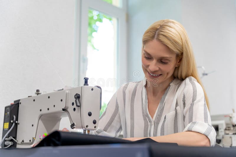 Blonde Cute Female Designer Sitting at the Sewing Machine and Looking ...