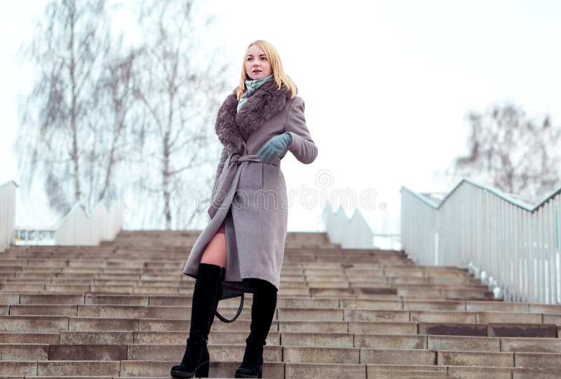 Blonde Girl In A Brown Coat With Fur And Long Boots Posing Standing On