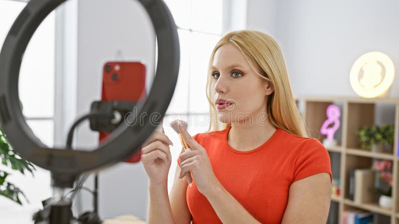 A Blonde Woman Applies Lipstick Indoors Using a Ring Light for a Beauty ...
