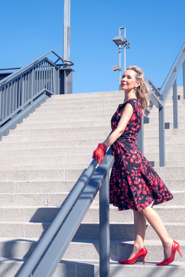 Blonde Woman In Red Dress Standing On Stair Steps And Enjoying The Sun