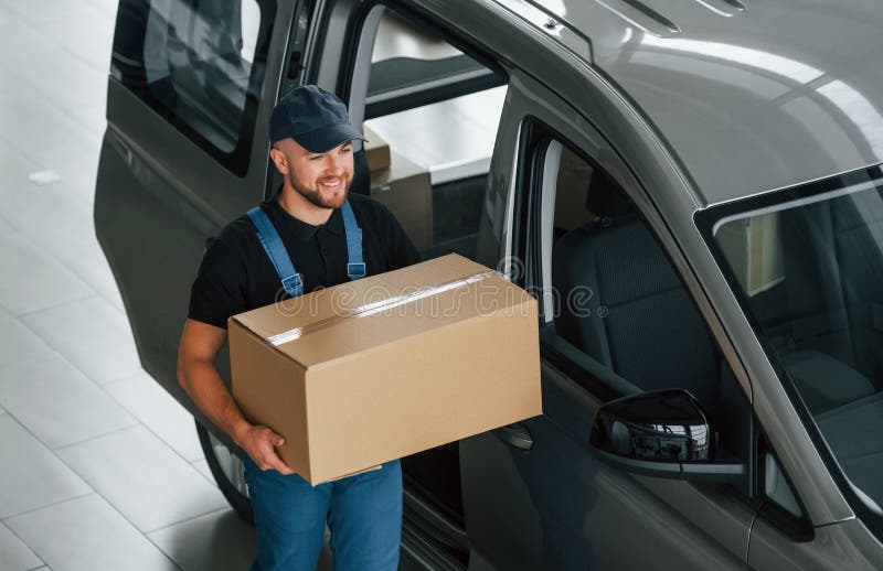 In Blue Colored Clothes. Delivery Man in Uniform is Indoors with Car ...