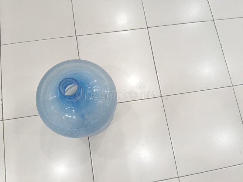 A Blue, Empty Plastic Water Bottle Gallon Jug on a White Tiled Floor ...