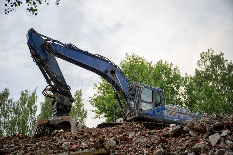 Blue Excavator Working on Demolition Site with Pile of Broken Bricks ...