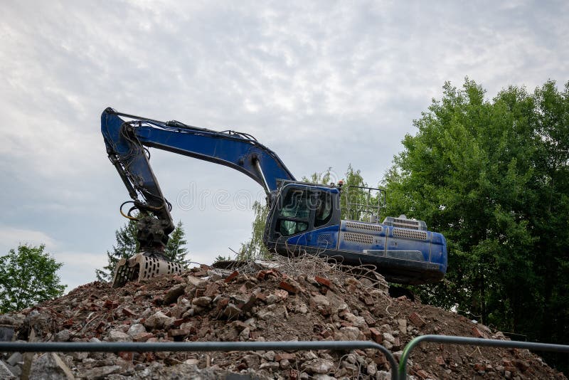 Blue Excavator Working on Demolition Site with Pile of Broken Bricks ...