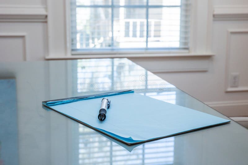 A Blue Notepad with a Pen Sitting on a Glass Top Table Near a Window in ...