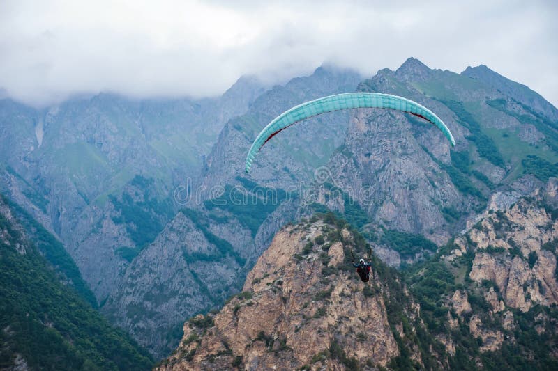 Blue Paraglider Flies Against a Background of Mountains and Clouds ...