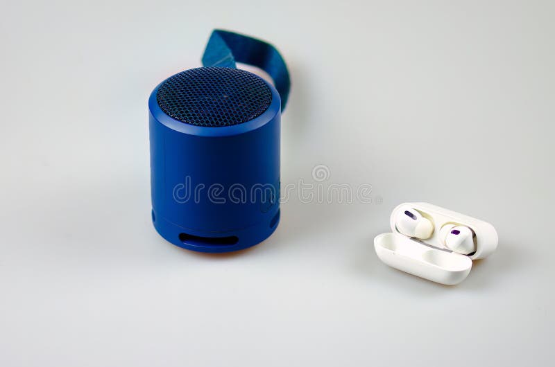 Blue Portable Speaker and White Wireless Earbuds on Light Surface Stock ...