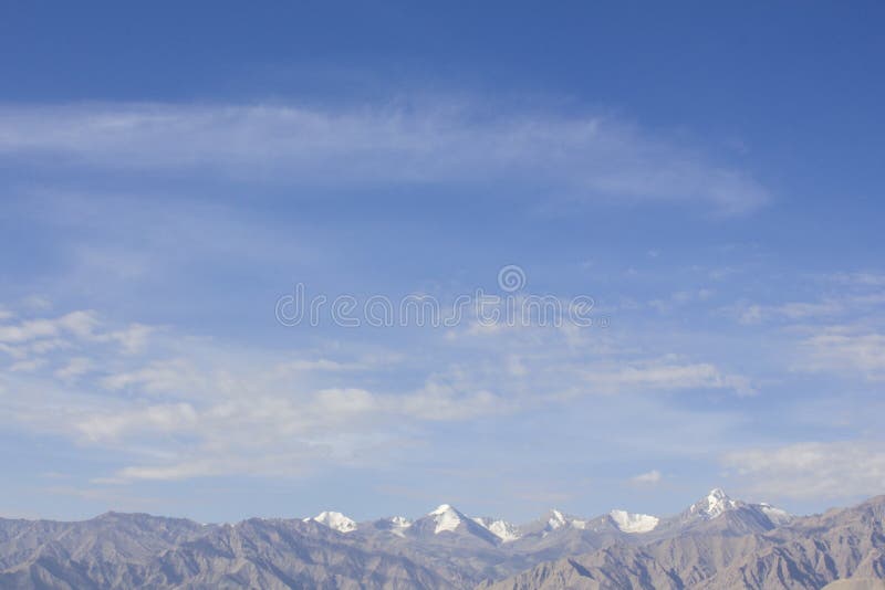 A Blue Sky with White Clouds Over the Desert Mountains with Snowy Peaks ...