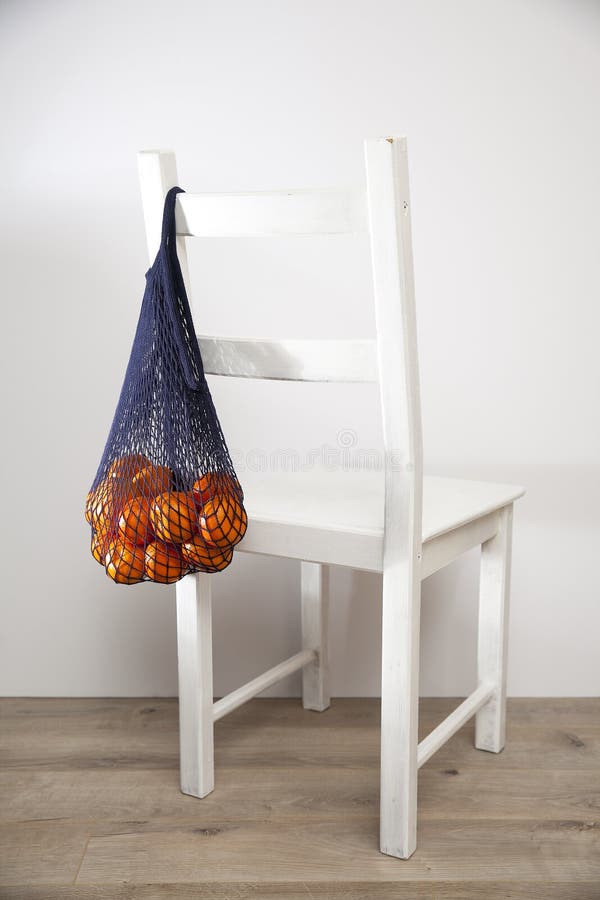 A Blue String Bag with Tangerines Hanging on Back of a White Chair ...