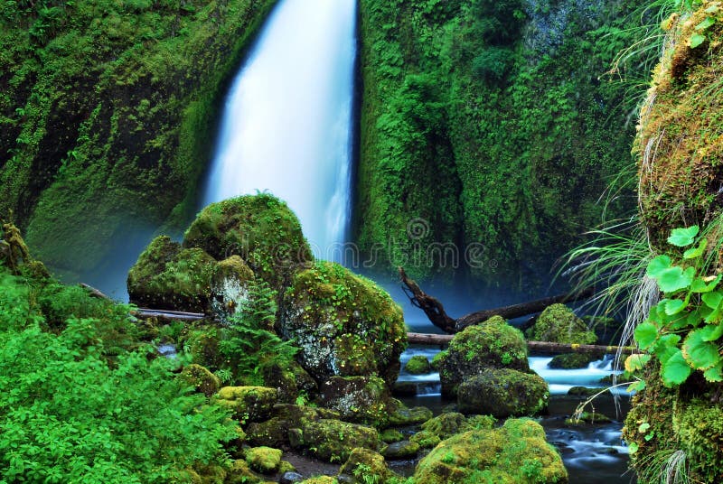 Blue Waterfall Flowing Down into a Green Valley Filled with Rocks and ...