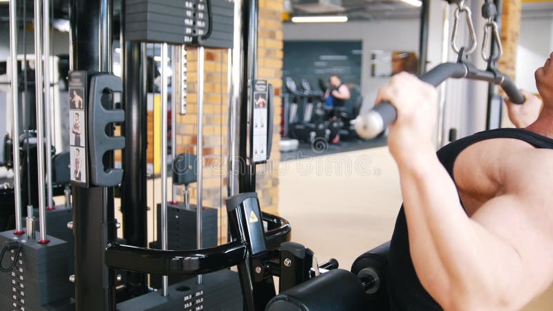 Bodybuilder in a Black Tank Top Performs an Exercise on Shoulder Pull ...