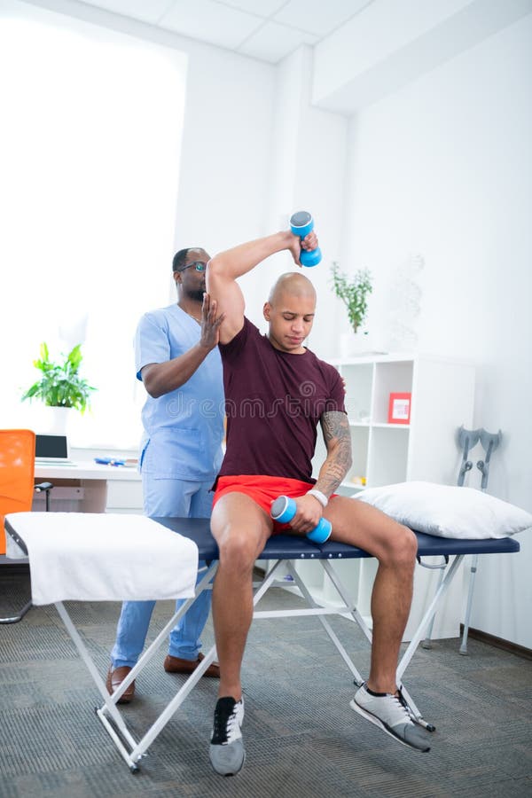 Bodybuilder Sitting and Doing Exercises with Barbells Near Therapist ...