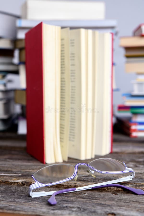 Book and Reading Glasses in Front of Piles of Different Books Stock ...