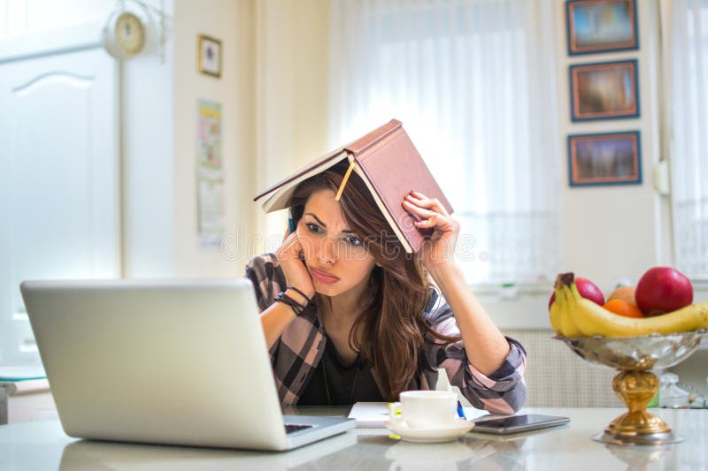 Bored Female Student Doing Homework on Laptop and Holding a Notebook on ...