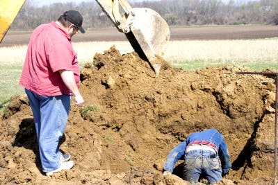 A city utilities forman watching an employee dig for a water line ...