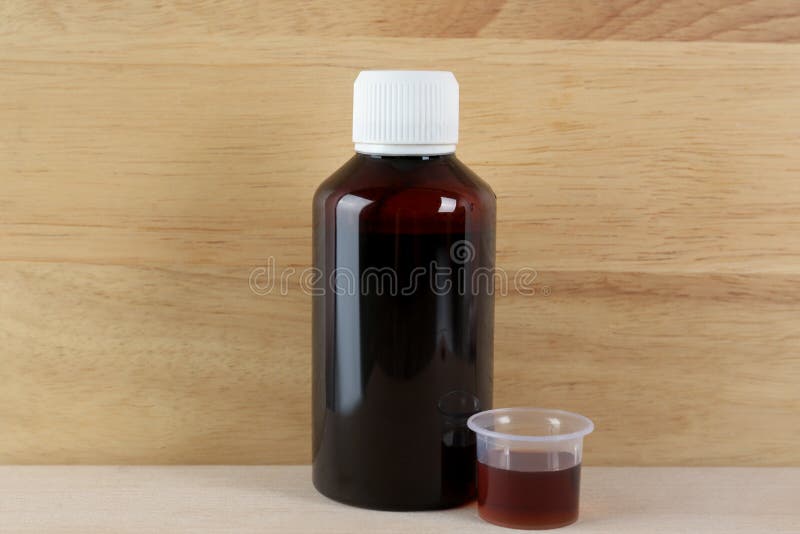 Bottle and Measuring Cup with Cough Syrup on White Table Against Wooden ...