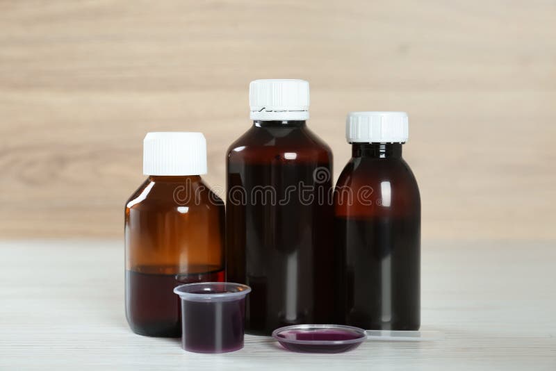 Bottles of Cough Syrup, Dosing Spoon and Measuring Cup on White Wooden ...