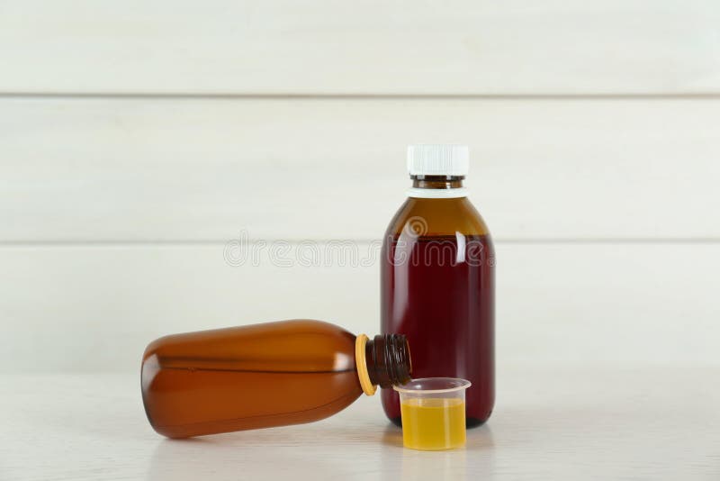 Bottles and Measuring Cup with Cough Syrup on White Wooden Table Stock ...