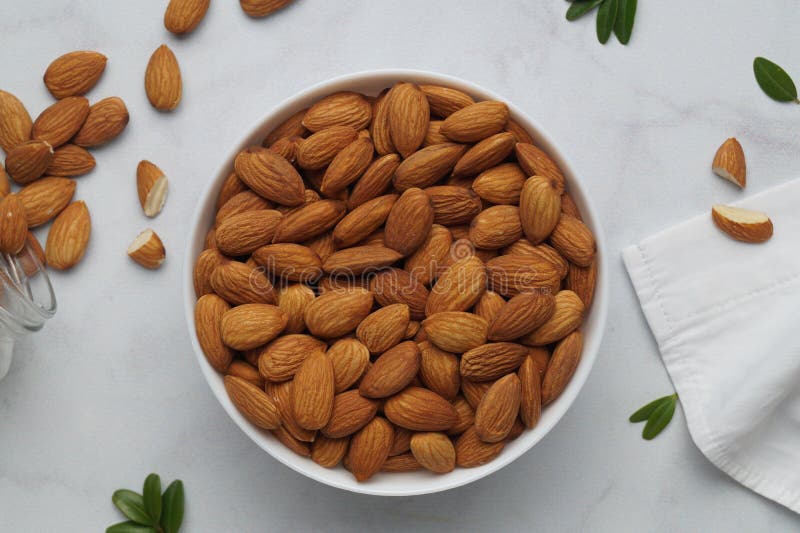 Bowl with Delicious Almonds and Fresh Leaves on White Marble Table ...