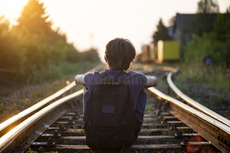 A Boy with a Backpack on His Back Sits on Train Tracks Stock Image ...