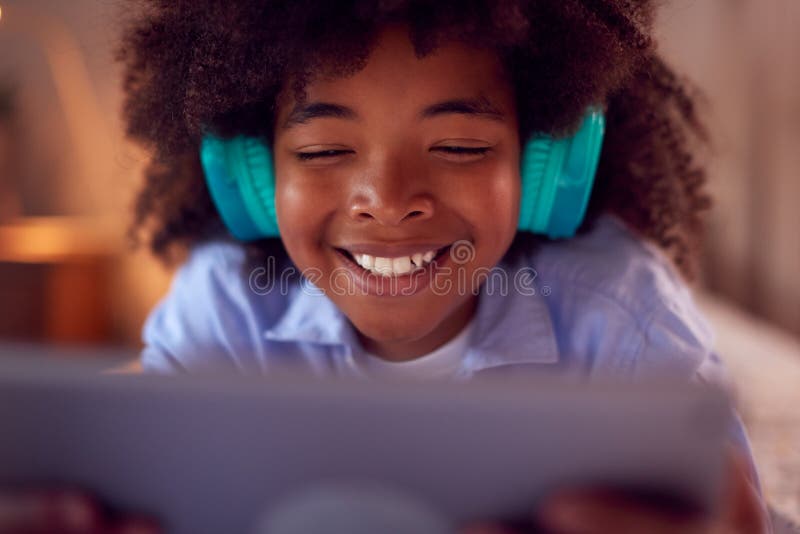 Boy in Bedroom Lying on Bed Wearing Headphones Using Digital Tablet ...