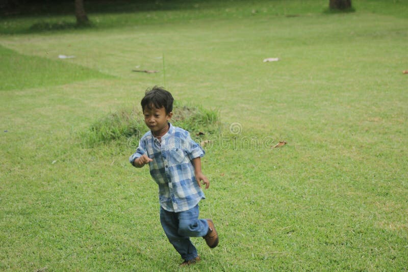 A Boy in a Blue Striped Shirt and Jeans is Running in the Park Stock ...