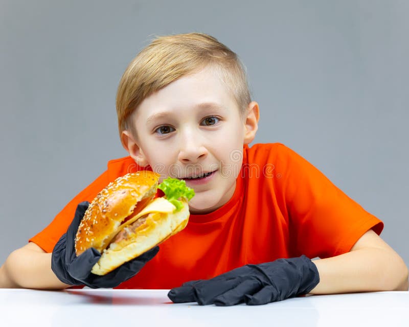 A Boy with a Cheeseburger Holds it in His Hand and Looks Straight Stock ...
