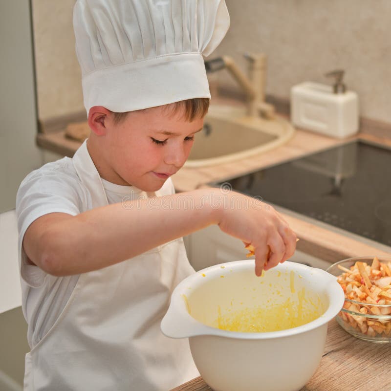 A Boy in Chef Clothes Pours Apples into the Dough for Cooking a Pie ...